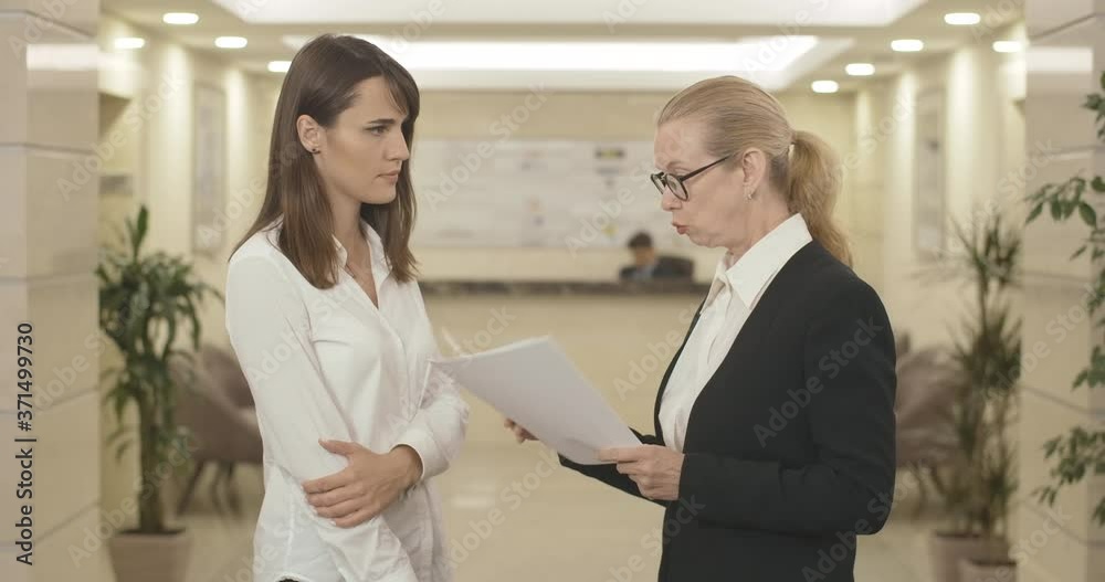 Angry mid-adult CEO scolding young female employee in business center ...
