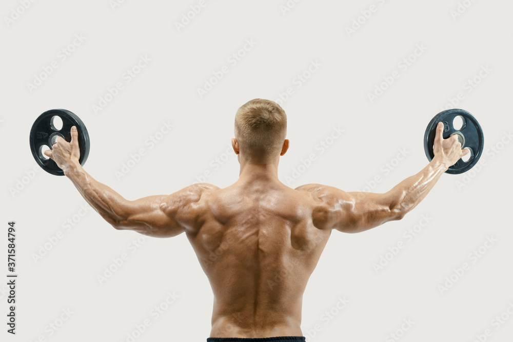 Rear view of young bodybuilder lifting weights rising hands against ...