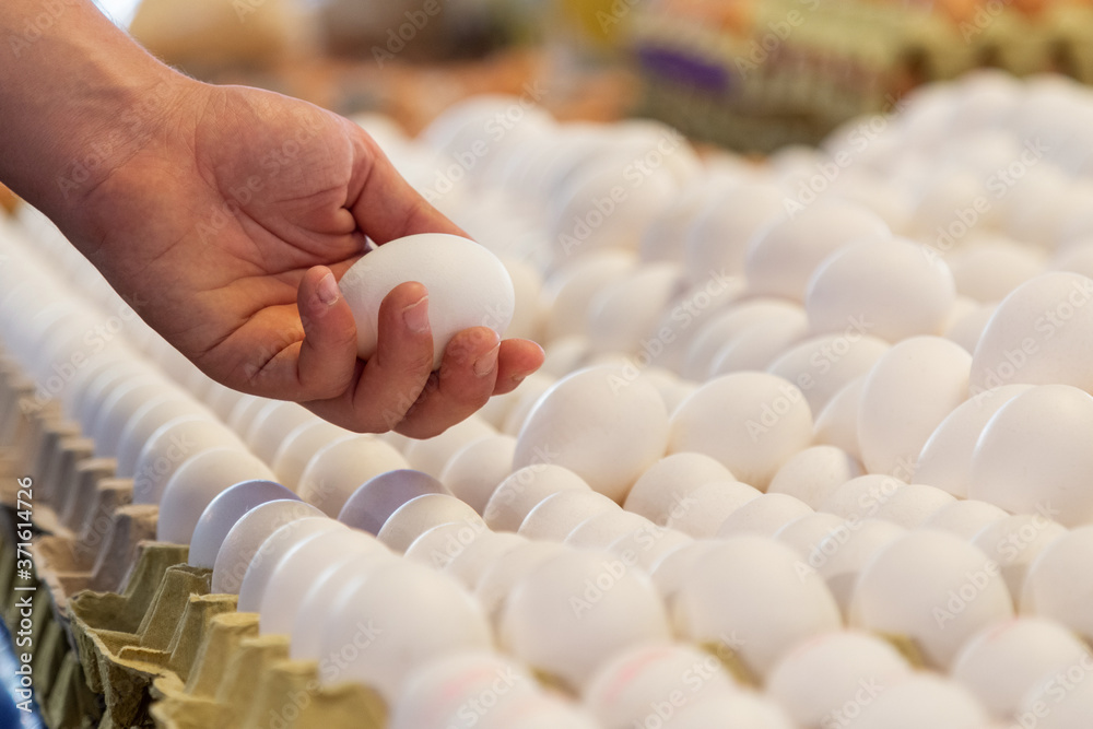 Shot of a hand of man picking up one fresh chicken egg from full egg ...