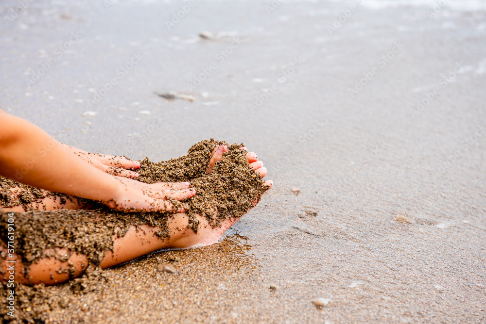 child plays on the beach in the sand. Baby hands and feet in the sand ...