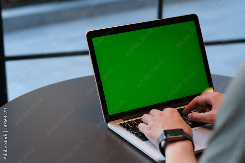 over shoulder of man using green screen laptop computer on table. blur ...