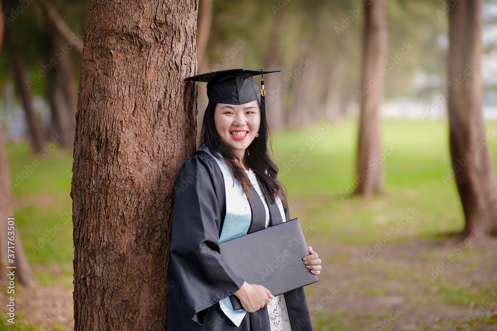 Happy Asian student holding degree certificate file while wearing gown ...