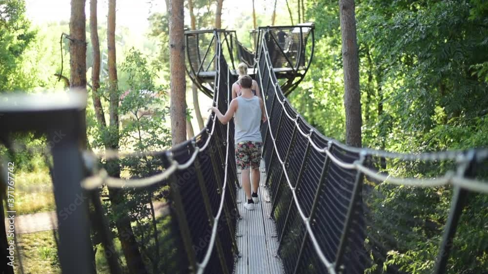 Young couple walks on treetop canopy footbridge. Unrecognisable people ...