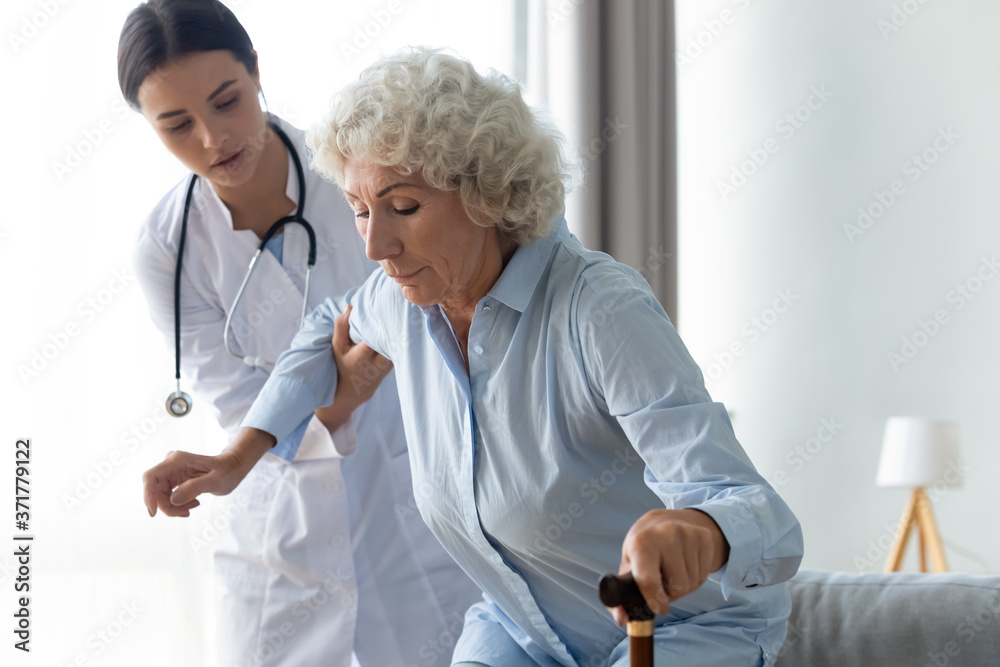 Careful young female physiotherapist helping older senior disabled ...