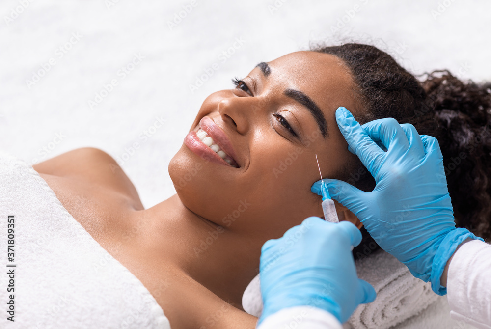 Smiling black woman having anti-aging injection for eye zone Stock ...