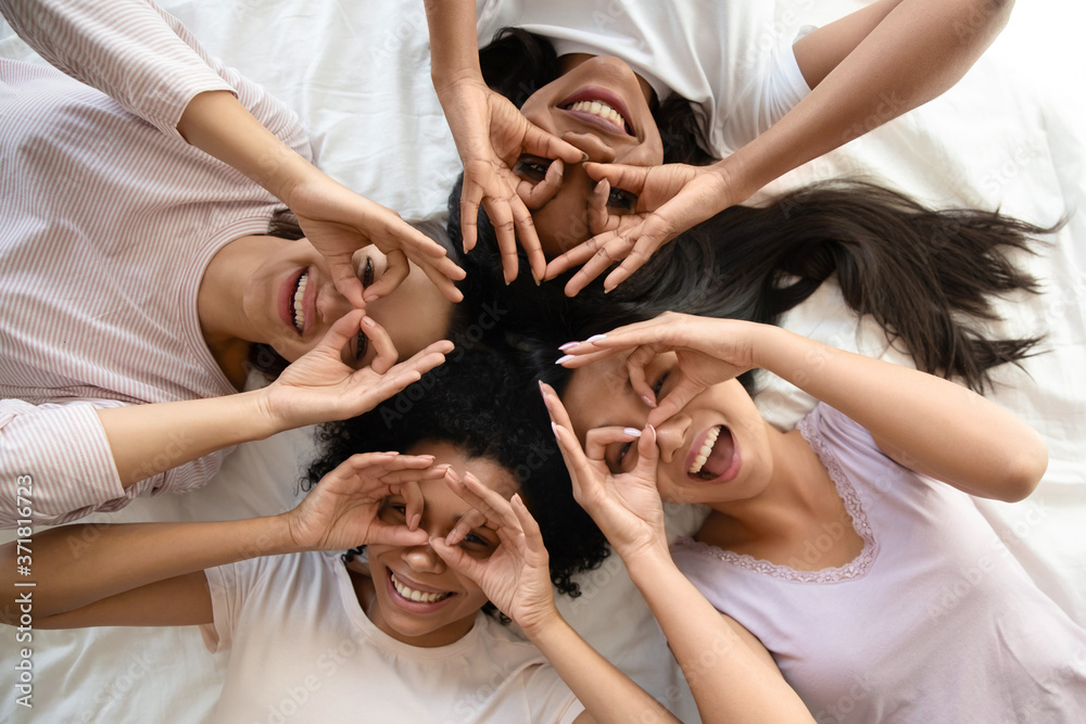 Group of cheerful diverse girls best friends lying in bed in pajamas ...