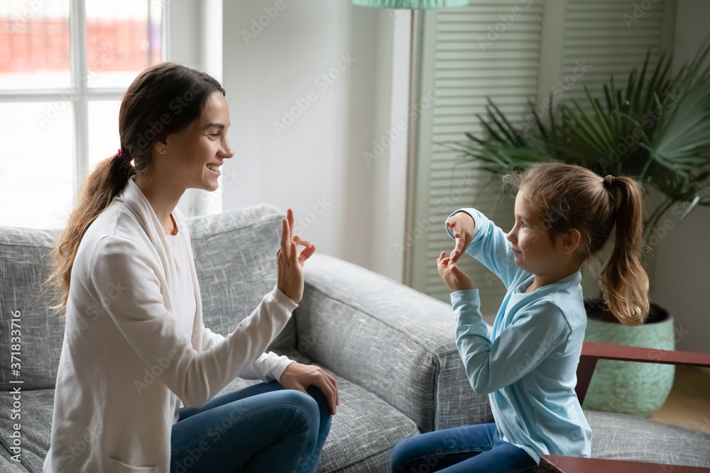 Smiling young mixed race woman teaching little cute girl sign language ...