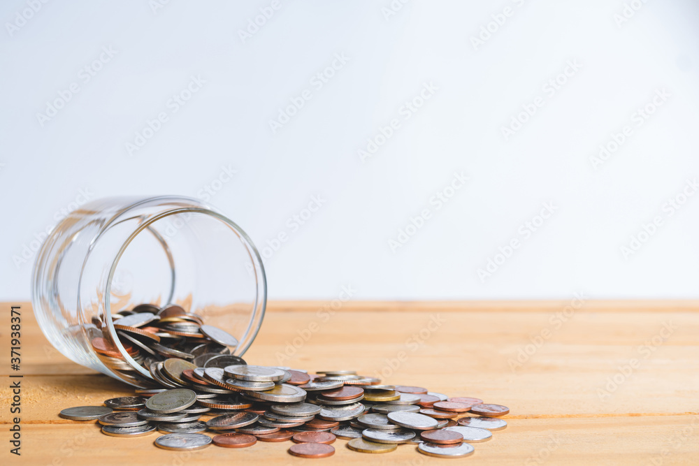 Coins in glass jar falling with money scattered on brown wooden table ...