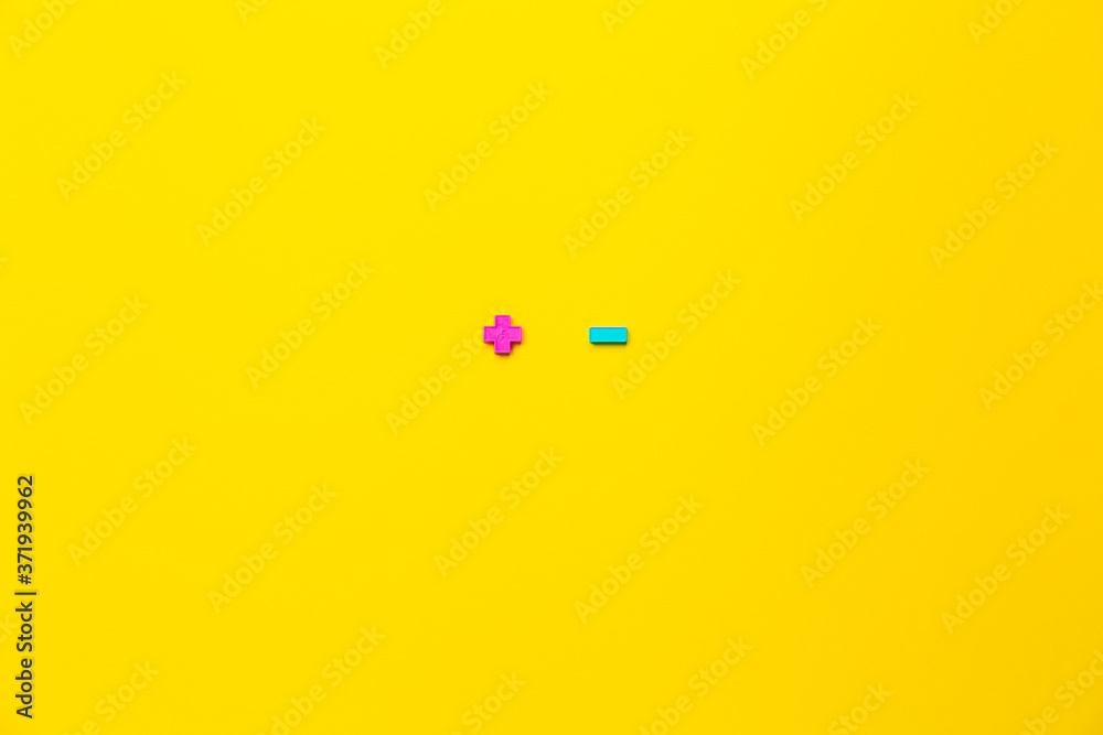 Plastic children's toy plus and minus signs on a yellow background ...