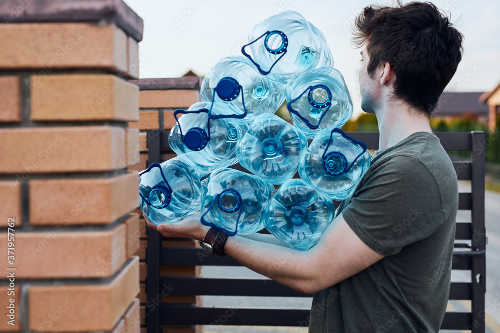 Young man throwing out empty used plastic water bottles into trash bin ...