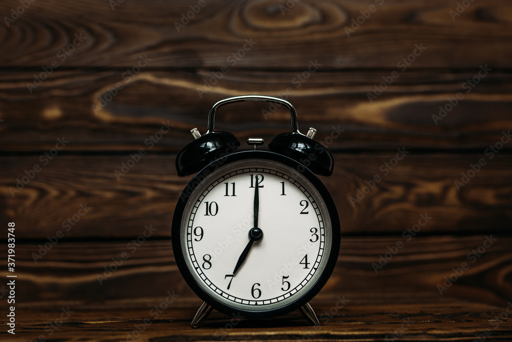 Clock on a wooden background. The clock shows the time of seven o'clock ...