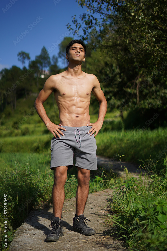 Young handsome shredded boy standing shirtless on the pathway. Fitness ...