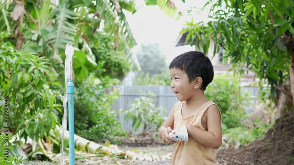 4K Asian child boy playing water splash from sprinkler in green natural ...