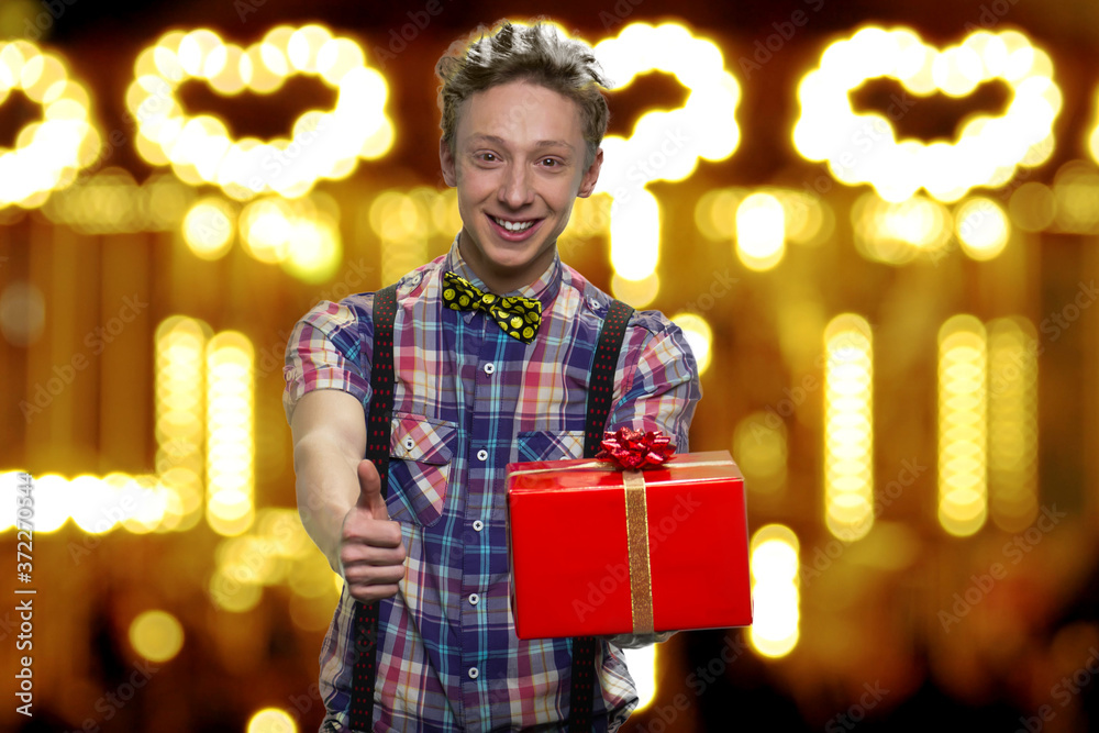 Smiling teen boy handing gift box to camera. Golden bokeh lights ...
