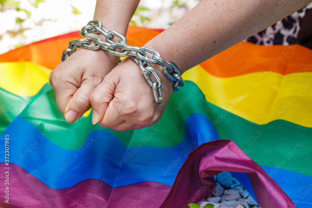 Female hands chained against the background of the LGBT flag. The ...