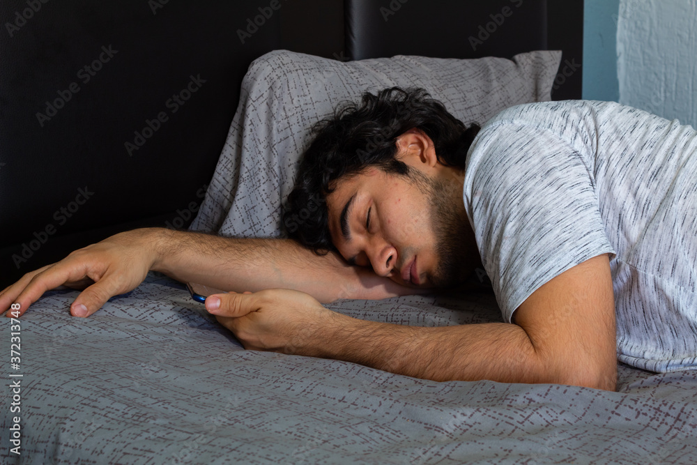Young hispanic man with long curly hair taking a nap on a bed with gray ...