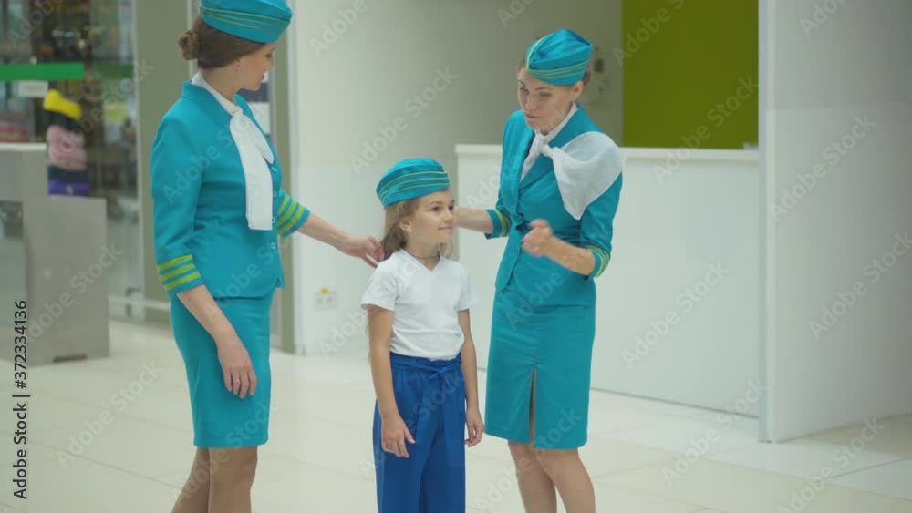 Smiling young woman putting stewardess hat on head of pretty little ...