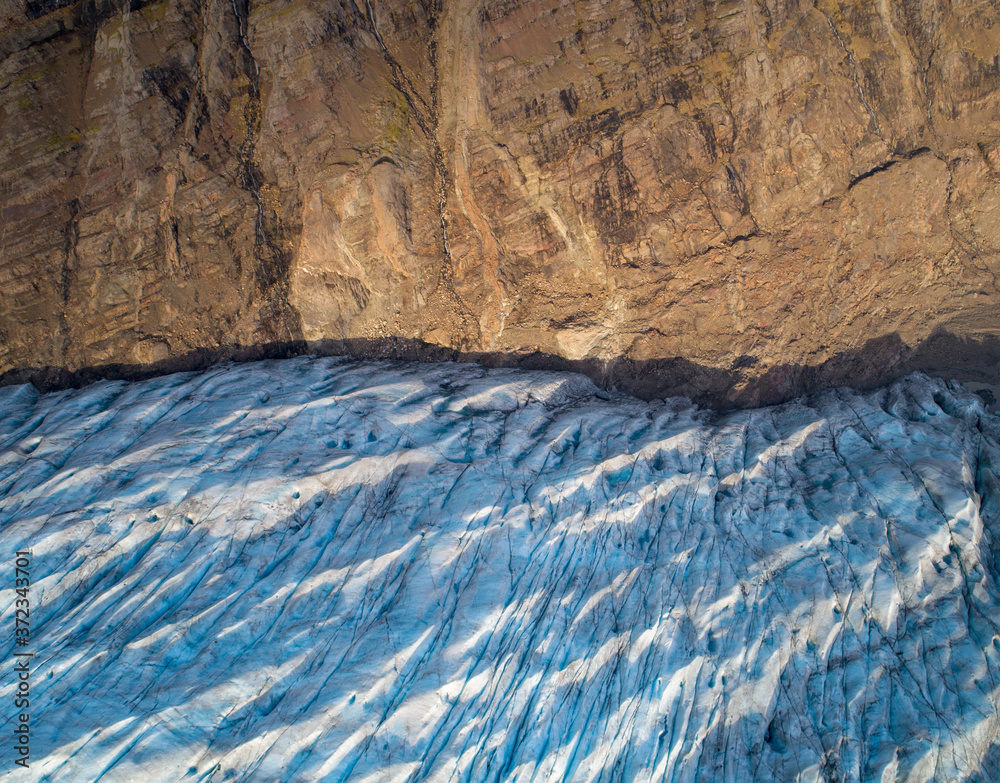 Aerial top view of the ridges of bleu and white glacier with black ash ...