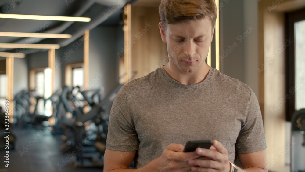Handsome sportsman texting message in sport club. Bodybuilder standing ...
