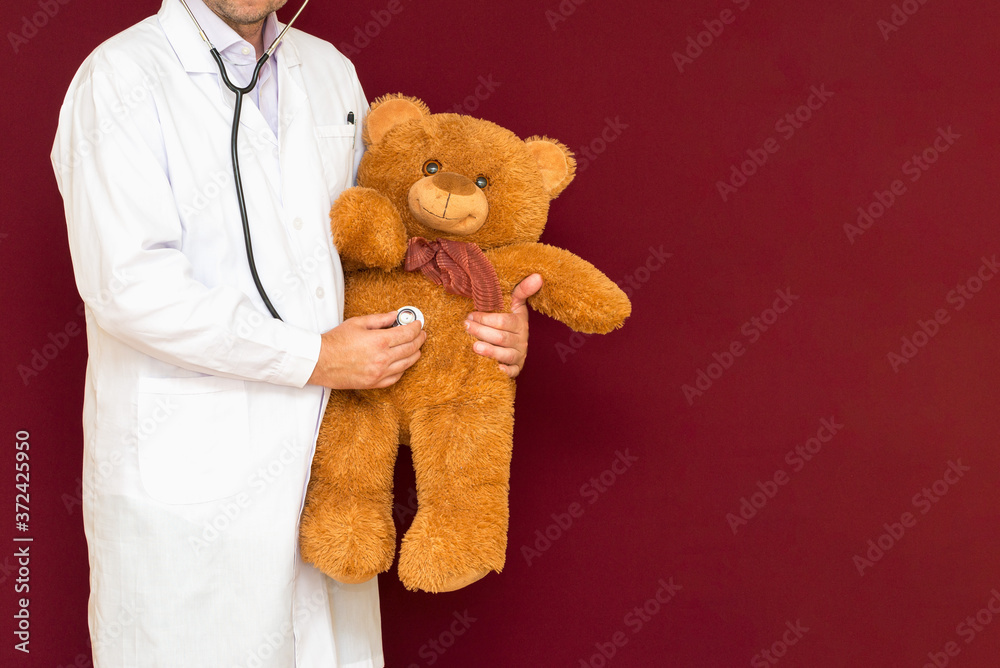 Pediatrician in a white coat, holds a brown teddy bear, doctor examines ...
