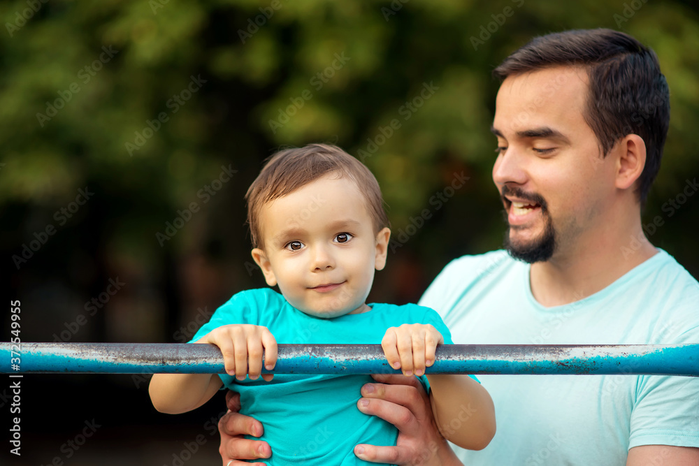 Father teaching toddler son to do pull ups exercise on steel bar ...