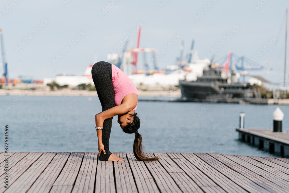 Female athlete practicing standing forward bend pose on pier against ...