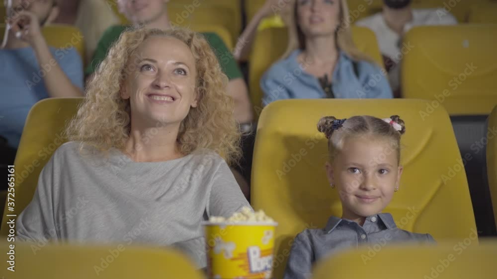 Embarrassed Caucasian mother closing daughter's eyes in cinema ...