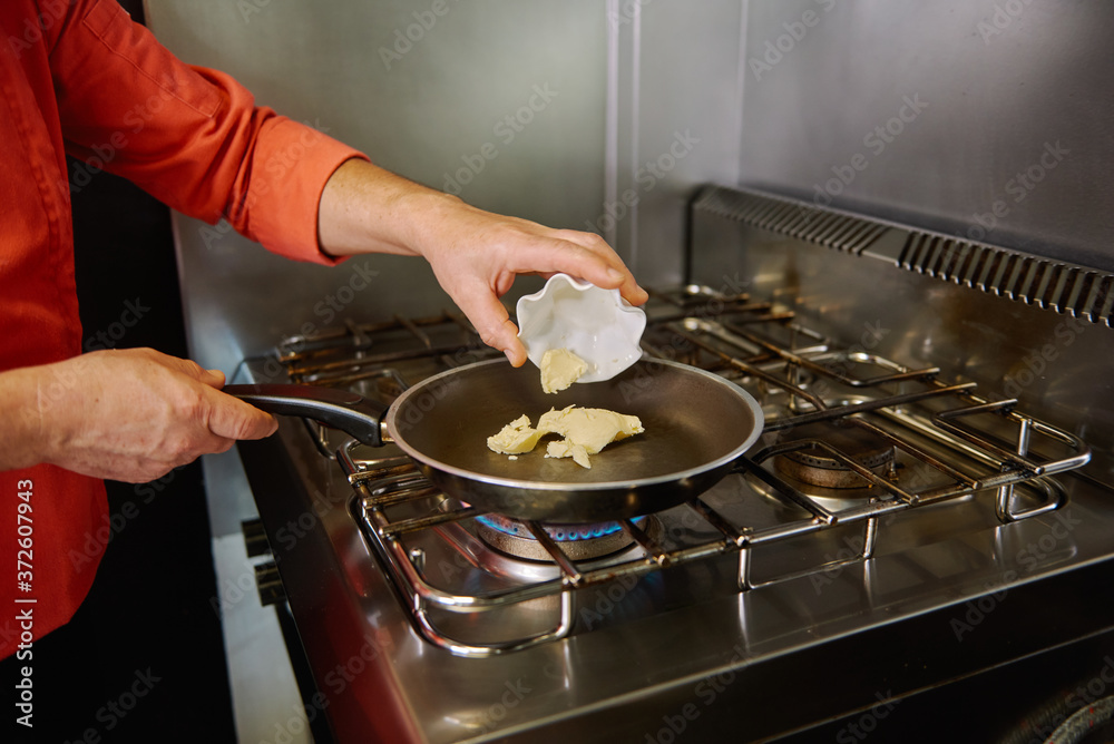 Crop anonymous chef adding butter pieces on frying pan from small ...