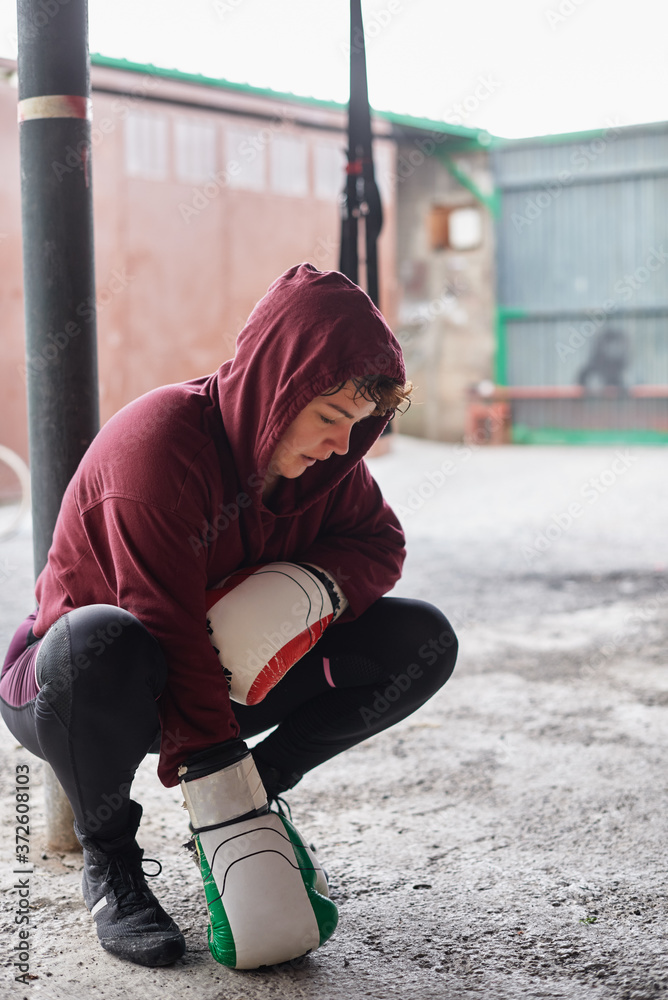 Full body determined exhausted female boxer in hoodie and boxing gloves ...