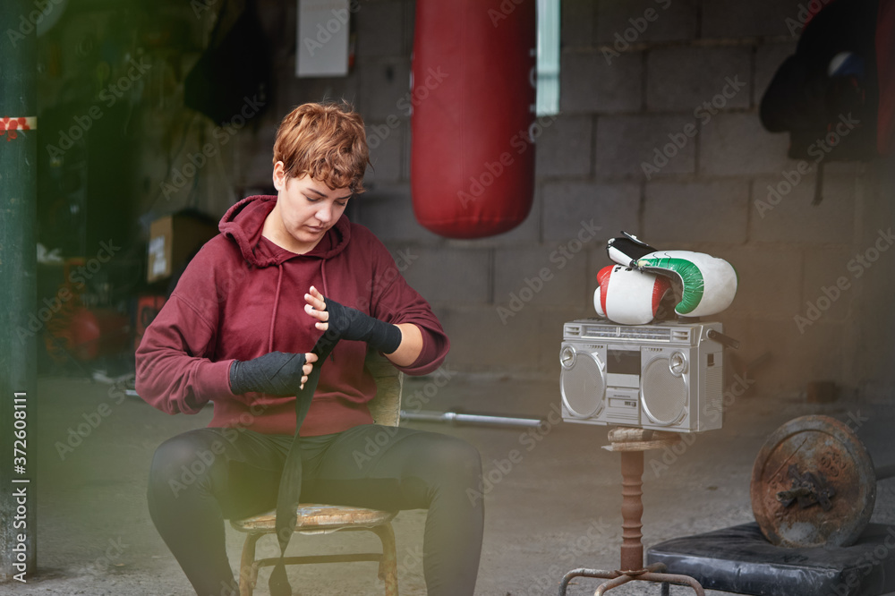 Crop concentrated female boxer in leggings and hoodie wrapping hands ...