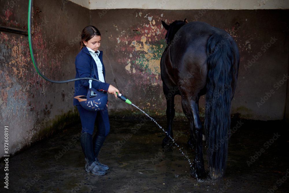 Side view of girl in rider clothes with helmet hanging on elbow washing ...