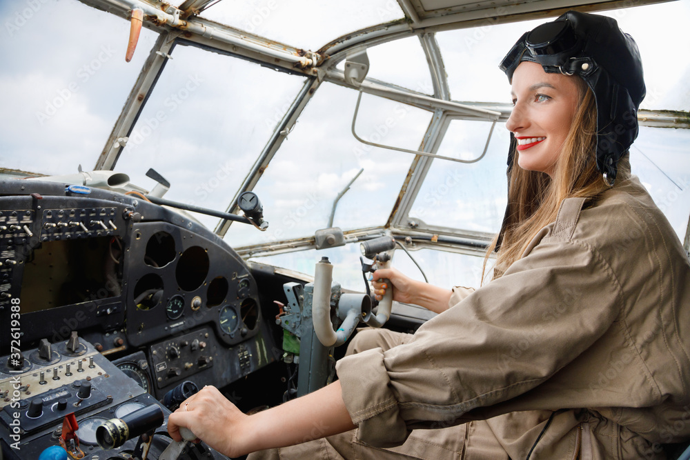Beautiful woman pilot in a helmet and pilot suit sits in the cabin ...