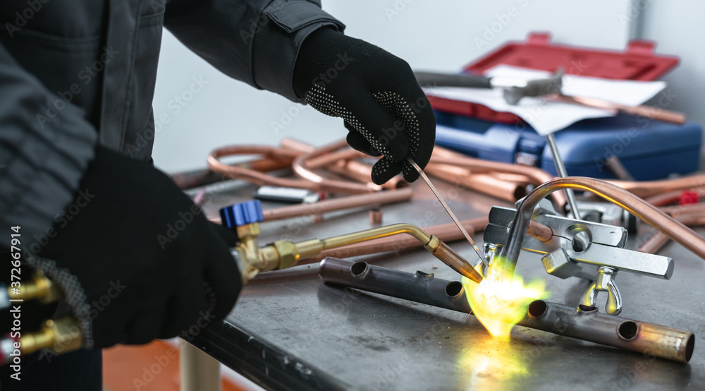 Worker is soldering a pipe by a blow lamp on a factory workbench ...