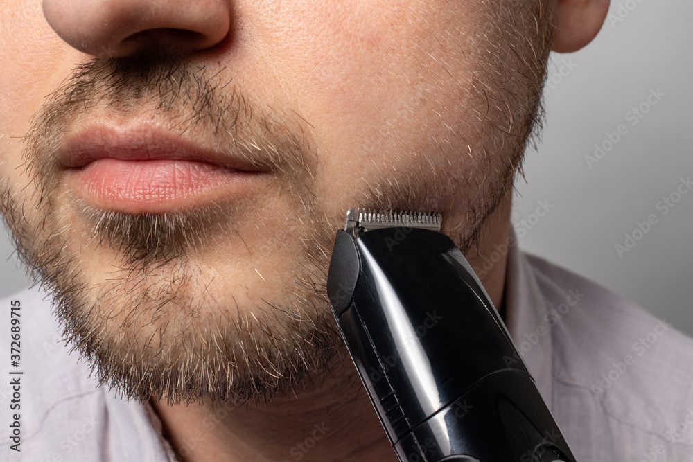 A man shaves his beard with a trimmer razor. Modeling beard, masculine ...