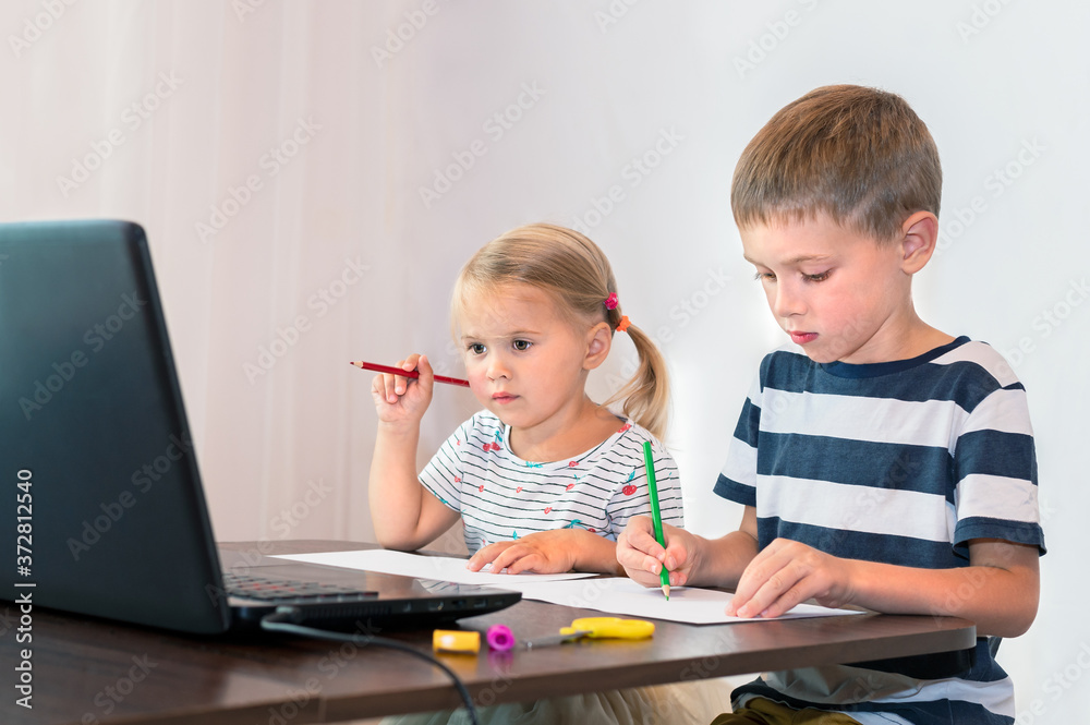 Brother and sister draw at home in front of their laptop. The concept ...