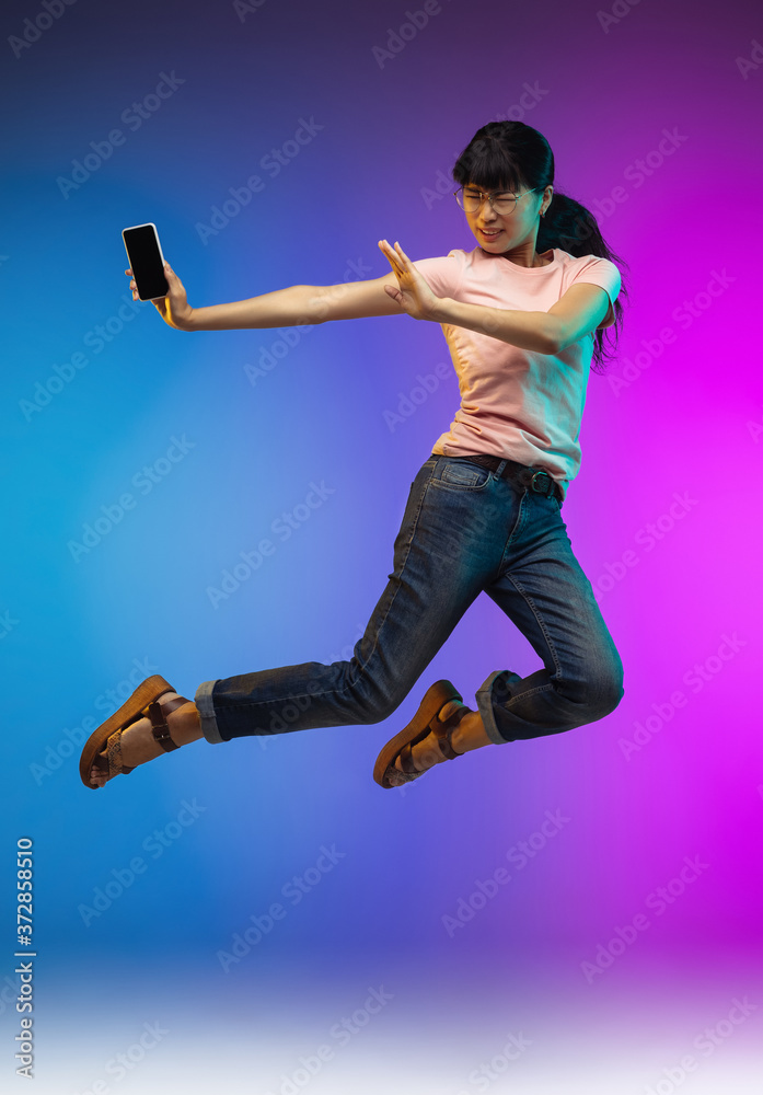 Giving phone. Jumping high asian young woman's portrait on gradient ...