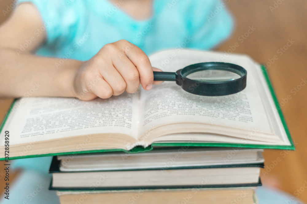 A person (child) looks at a book through a magnifying glass (loupe). A ...