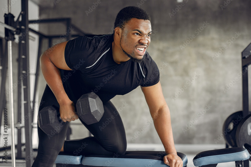 Sports man in the gym. A black man performs exercises. Guy in a black t ...