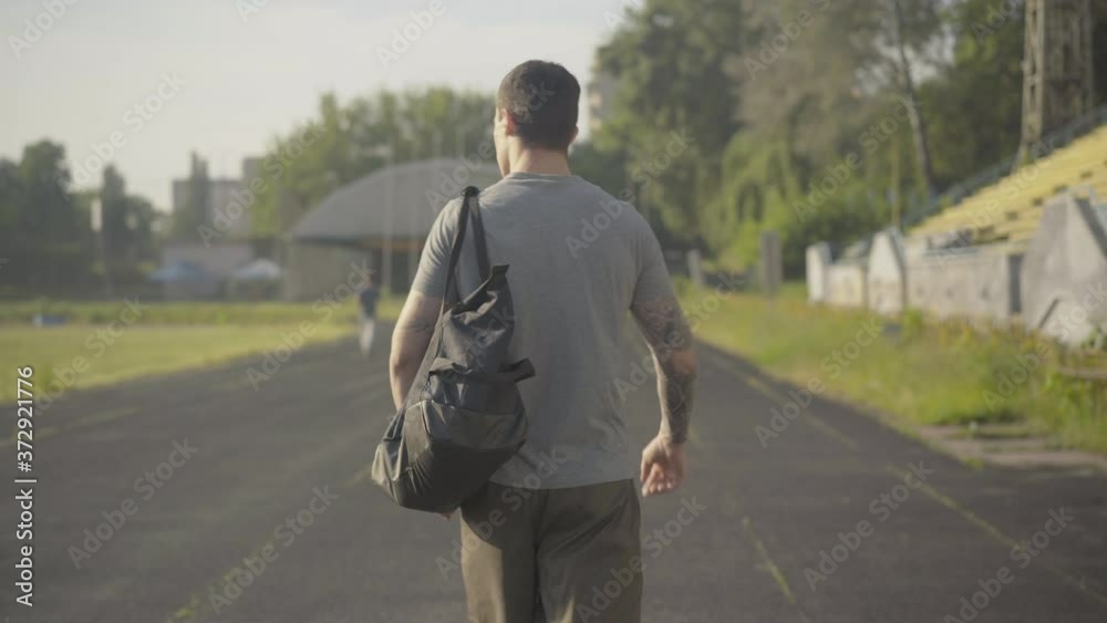 Back view of confident Caucasian man with sport bag walking along ...