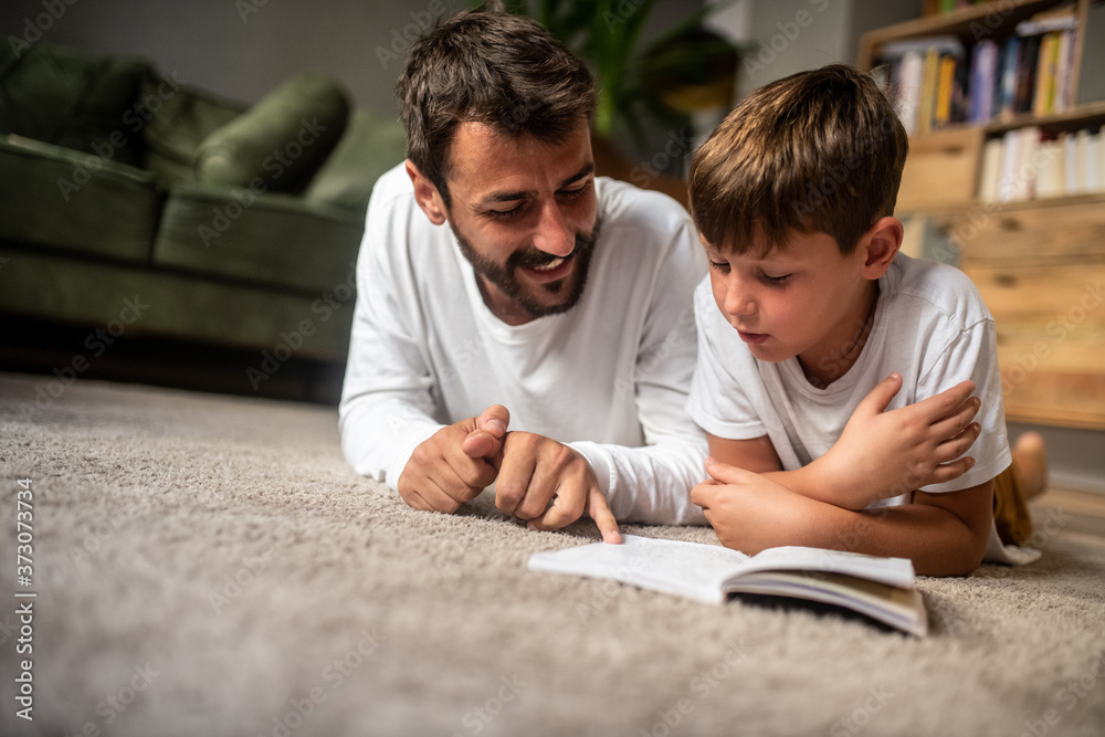 Father and son read a book together, father smiles while son reads ...