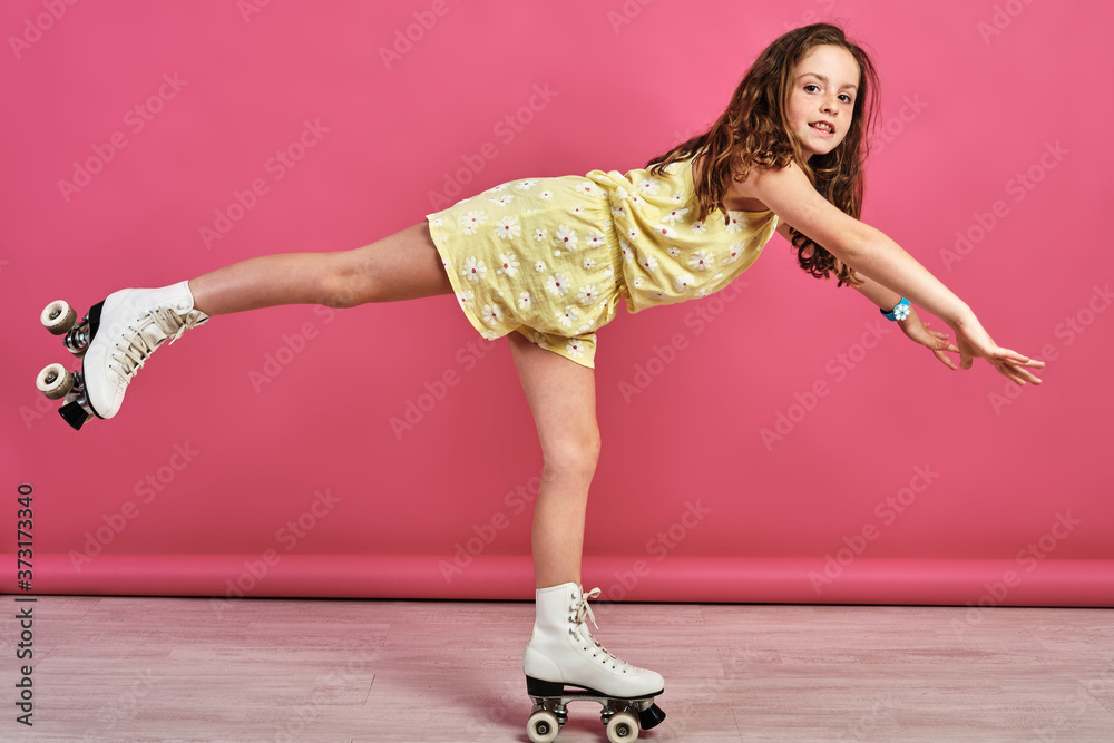 Little girl doing tricks with roller-skates in a studio with a pink ...