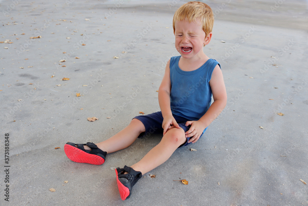 Sad boy having abrasions on his leg. Child injured his knee on the ...