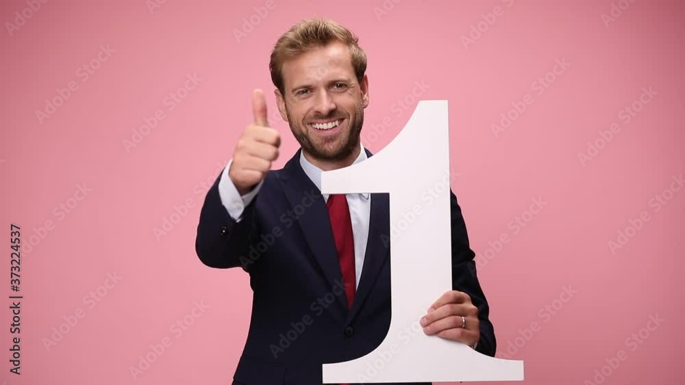 smiling young fashion model in navy blue suit holding number one sign ...