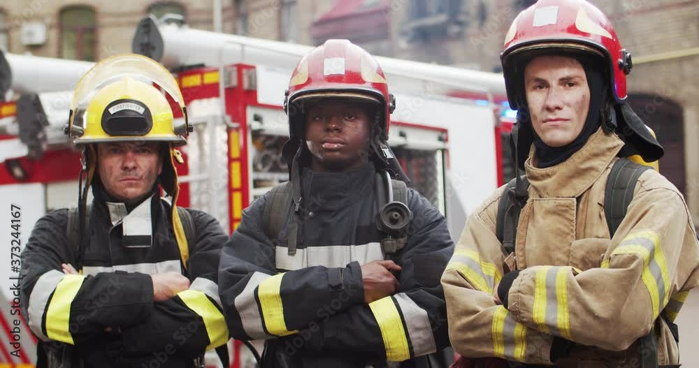 Portrait of three firefighters standing next to fire van in front of ...