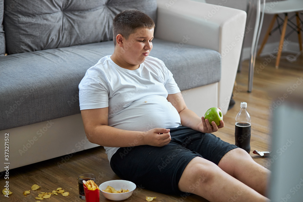 an overweight child boy enjoy leading unhealthy passive lifestyle, sits ...