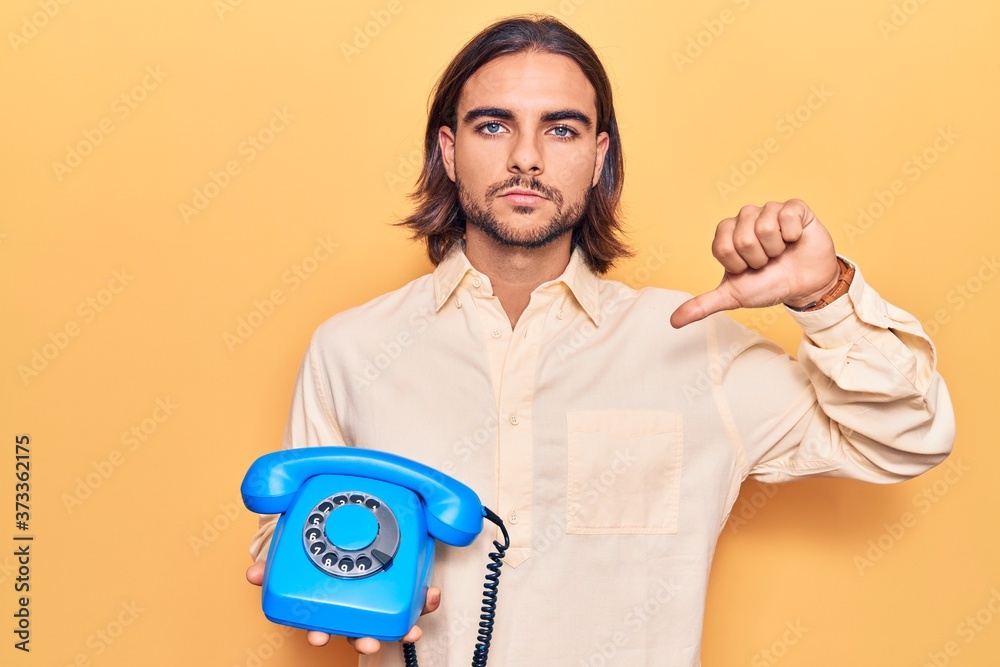 Young handsome man holding vintage telephone with angry face, negative ...
