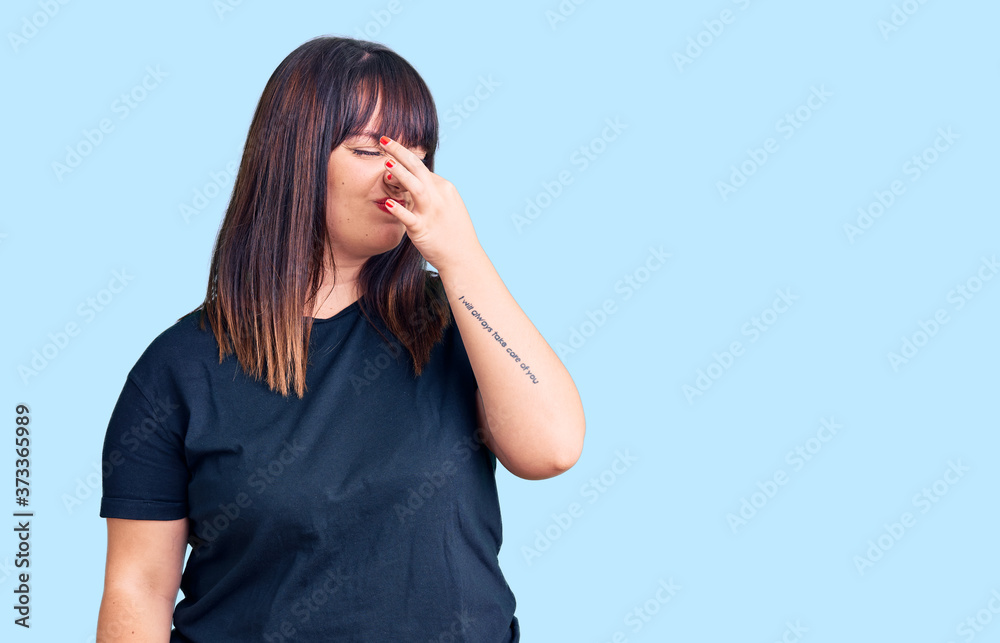 Young plus size woman wearing casual clothes smelling something stinky ...
