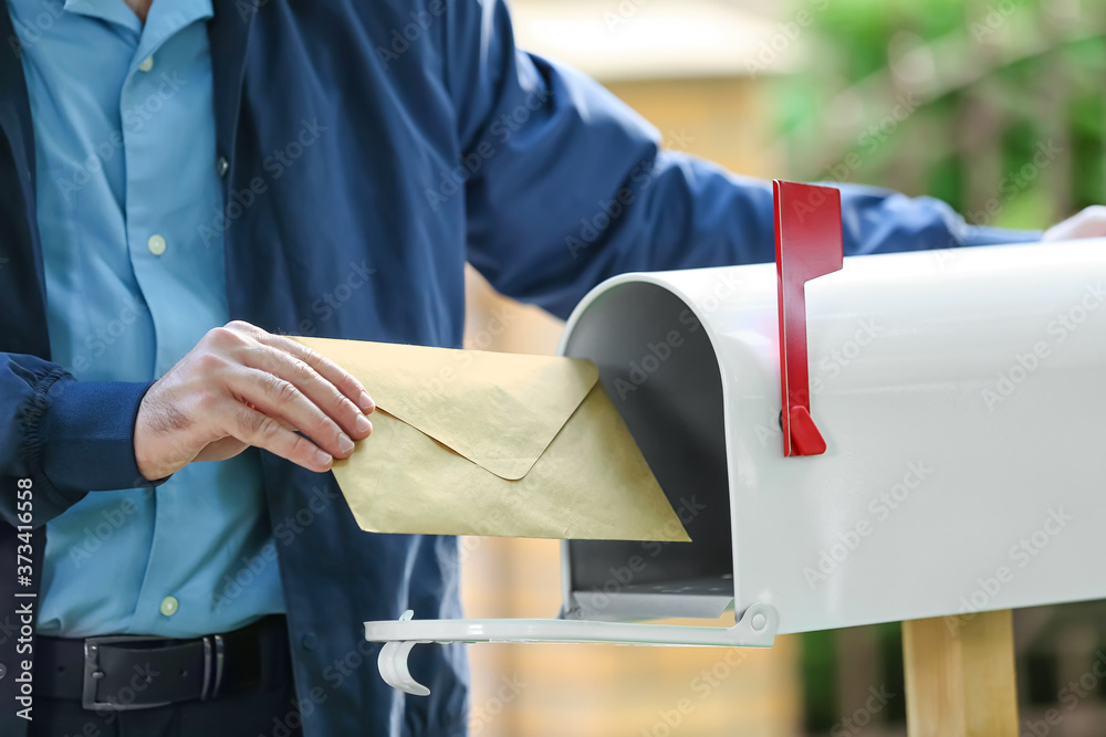 Handsome young postman putting letter in mail box outdoors Stock Photo ...