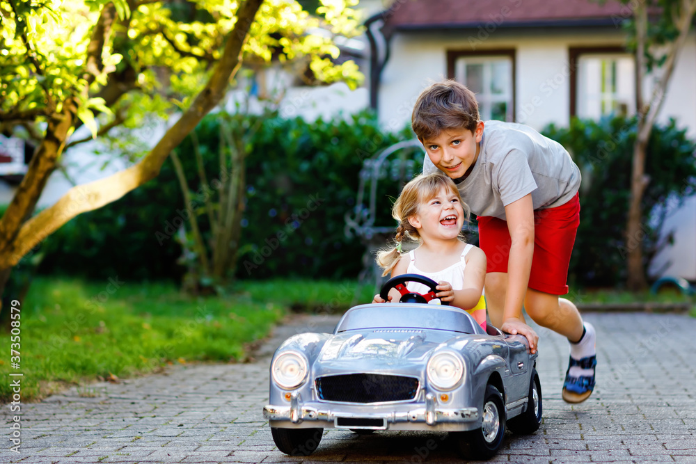 Two happy children playing with big old toy car in summer garden ...