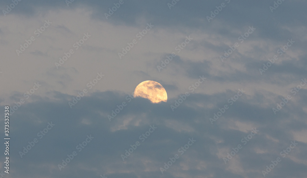 August orange full moon hides behind blue clouds background, texture ...